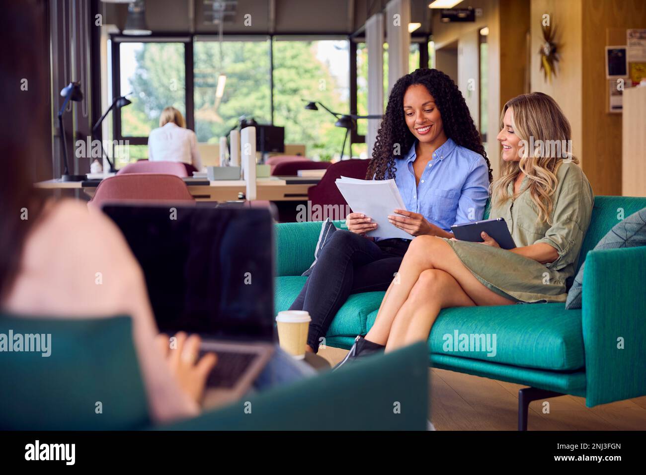 Businesswomen Having Informal Meeting In Breakout Seating Area Of ...