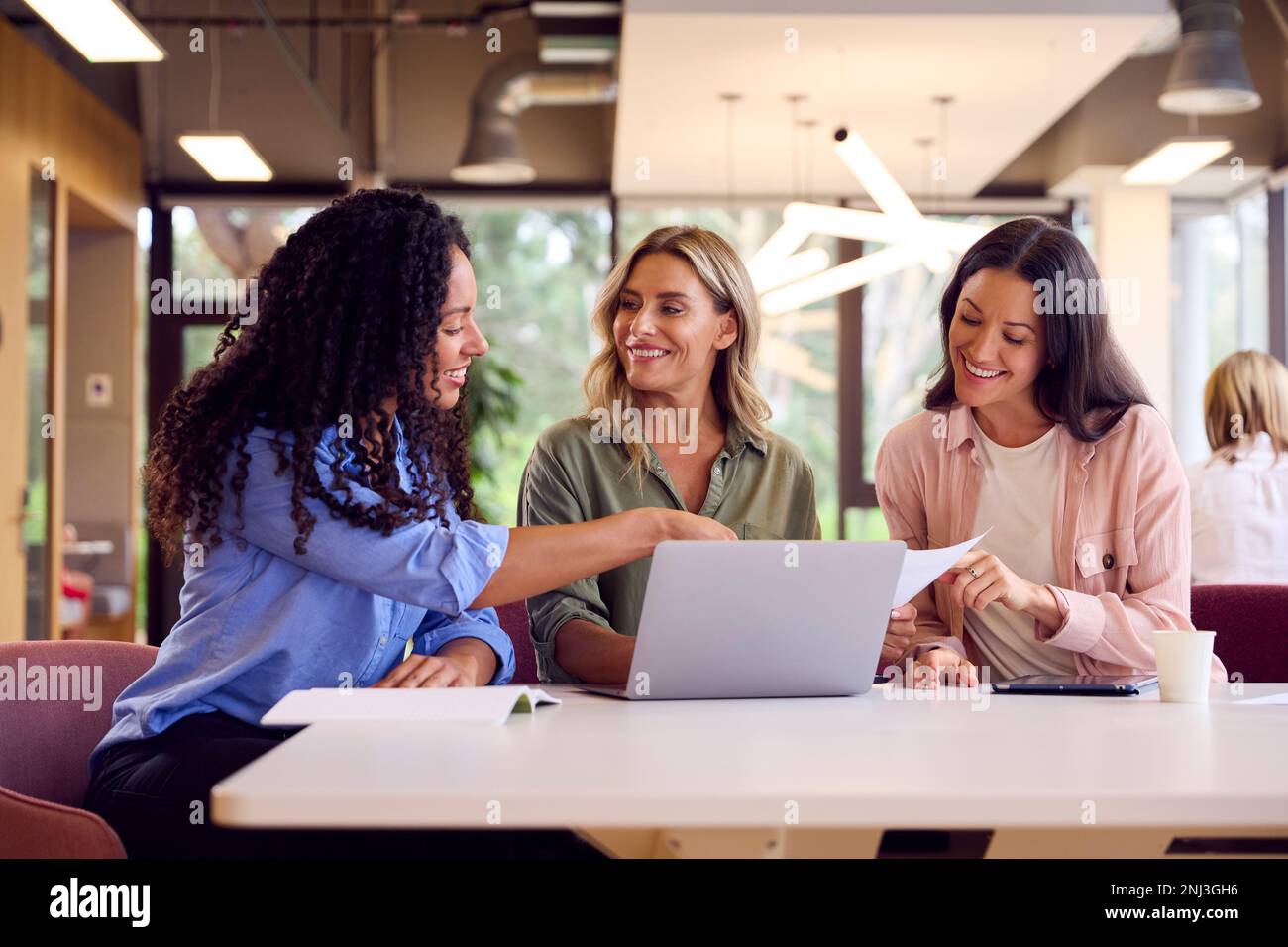 Multi-Cultural Female Business Team Sitting At Desk In Open Plan Office ...
