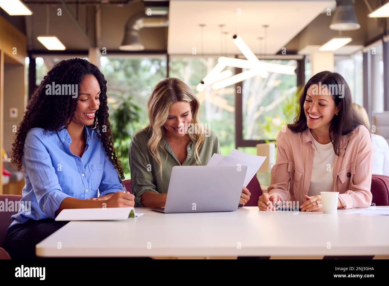Multi-Cultural Female Business Team Sitting At Desk In Open Plan Office ...
