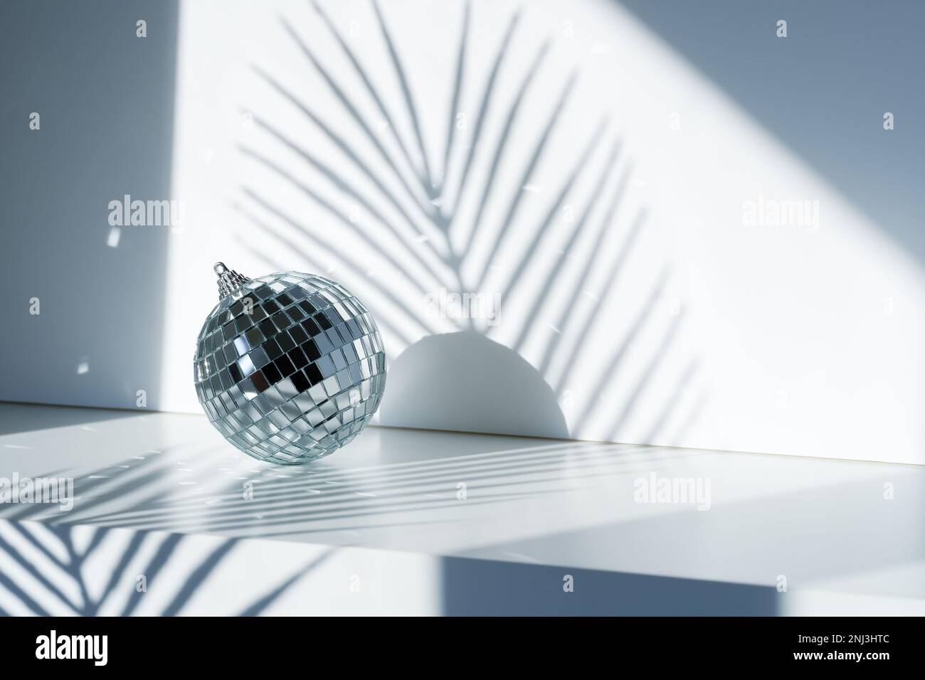 Disco ball in sunlight with geometric palm leaf shadow and reflections ...