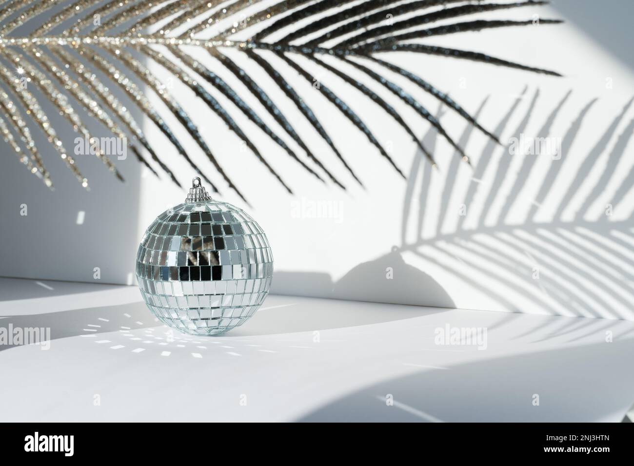 Disco ball in sunlight with geometric palm leaf shadow and reflections ...