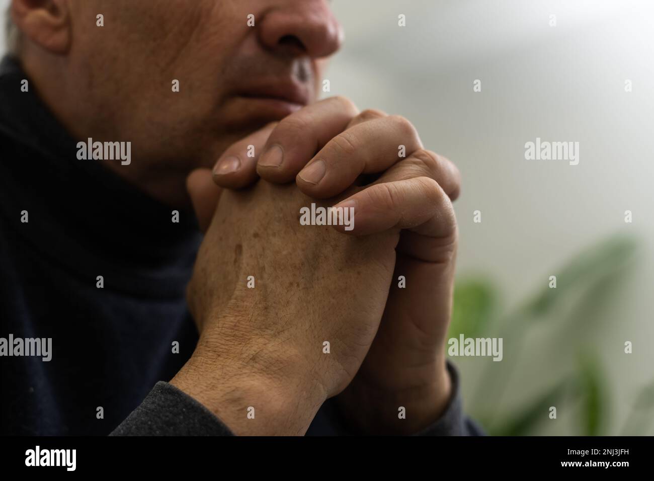 Worried religious senior man praying to god with his hands raised and ...
