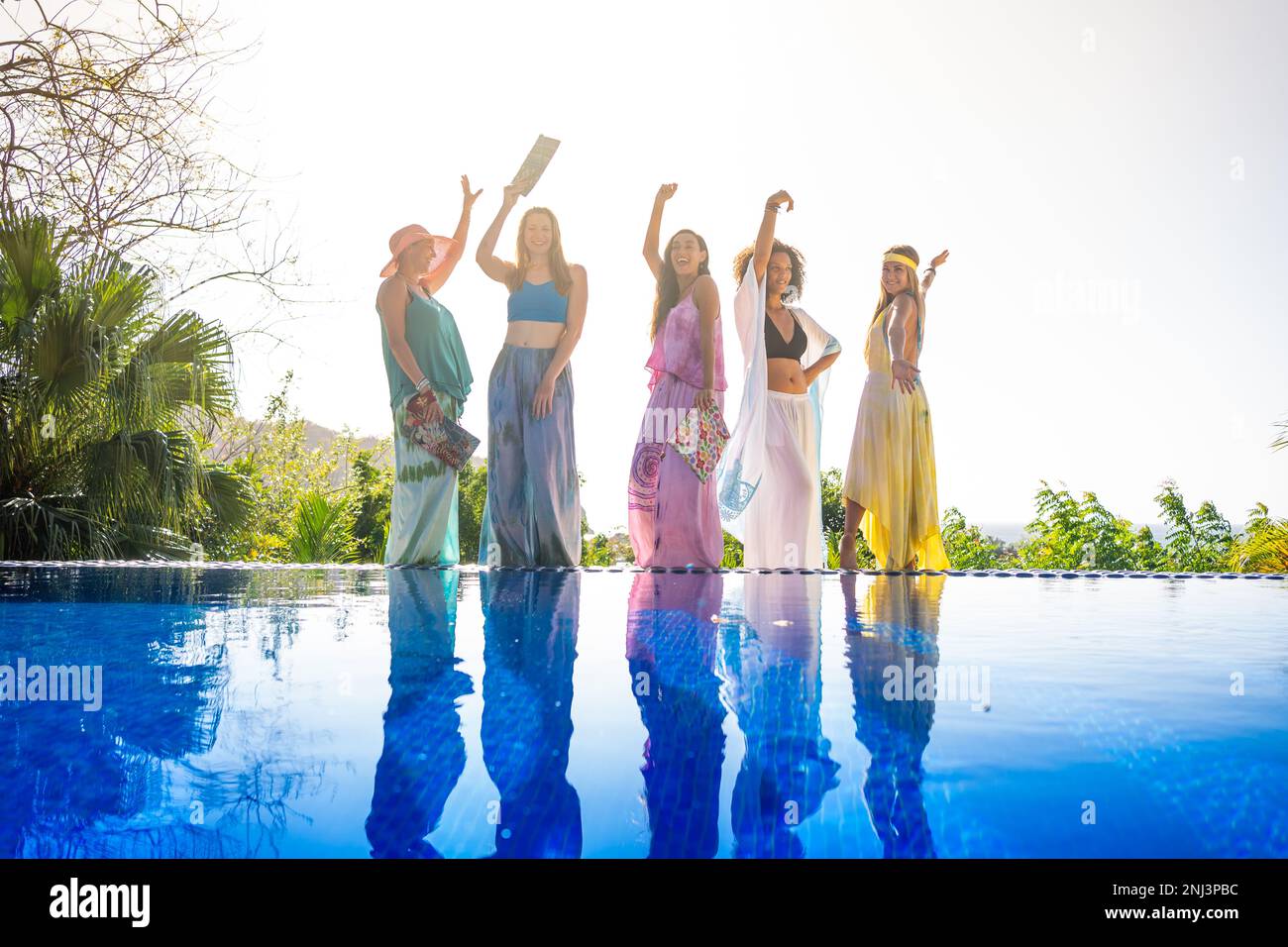 Four models posing on the edge of an outdoor tropical pool with the ...