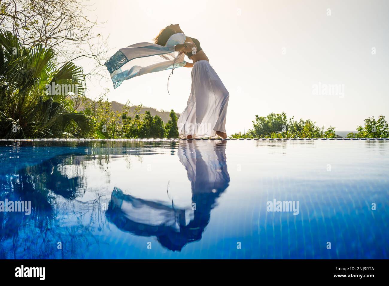 Model dancing on the edge of an outdoor tropical pool with the image ...