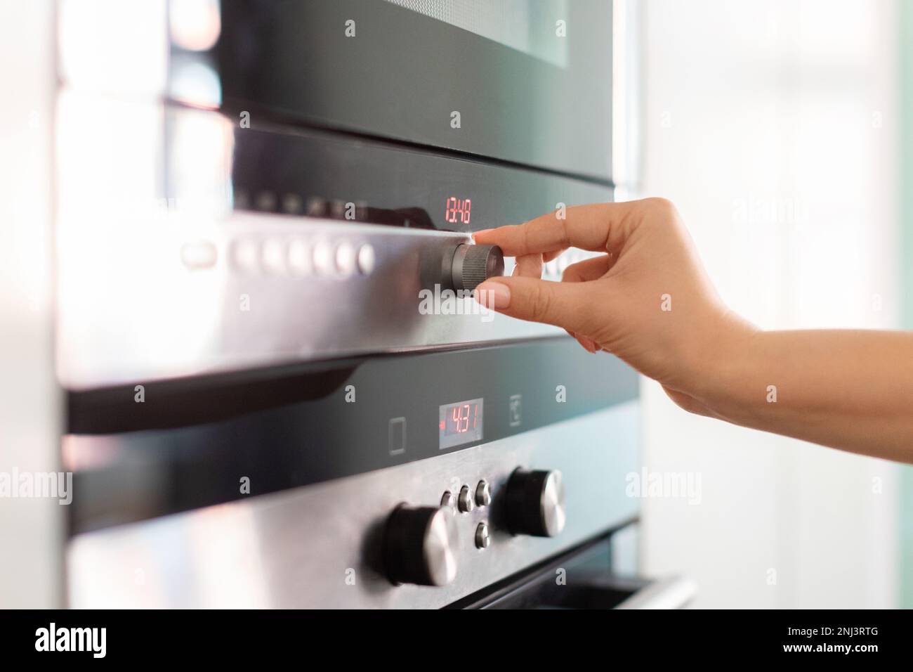 Female hand adjusting temperature on electric oven while cooking in ...