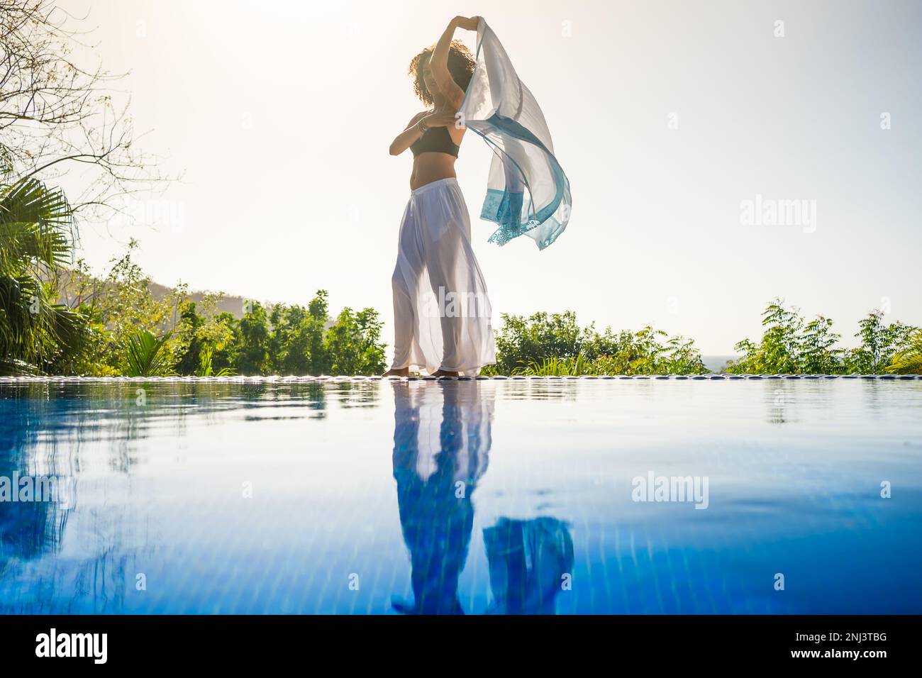 Model dancing next to an outdoor tropical pool with the image reflected ...