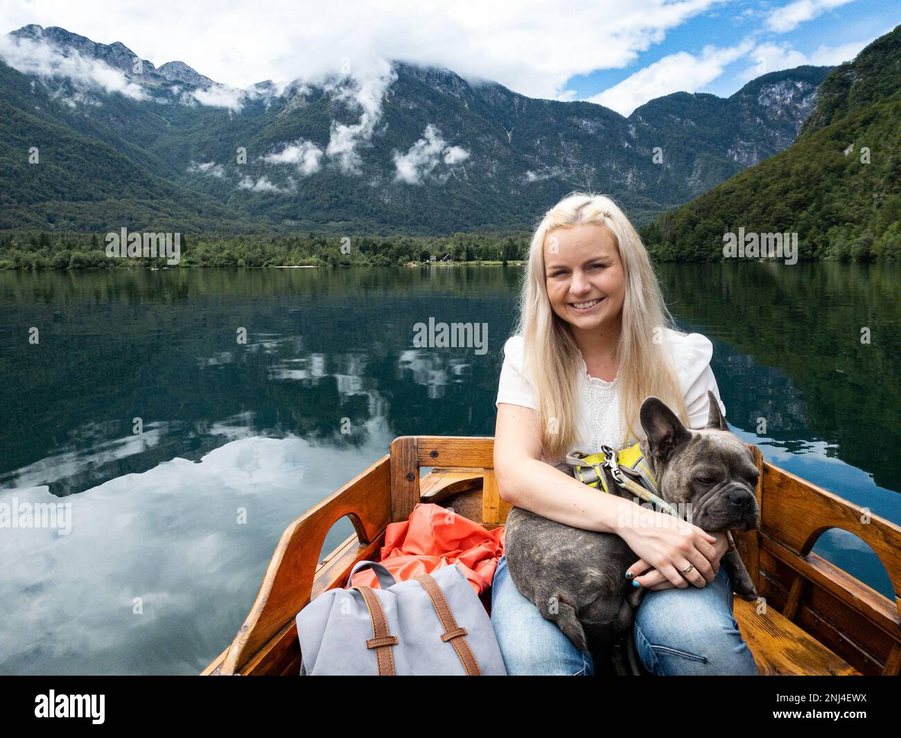 Woman with a french bulldog on her lap sitting in a row boat on a lake ...