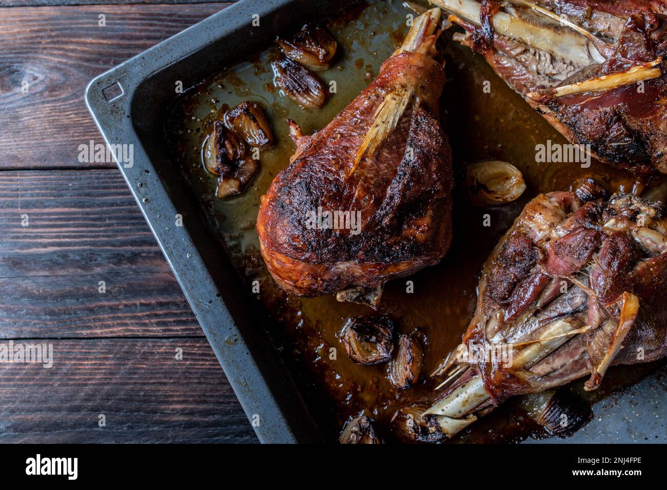 Oven roasted turkey legs on a baking tray isolated on dark wooden ...