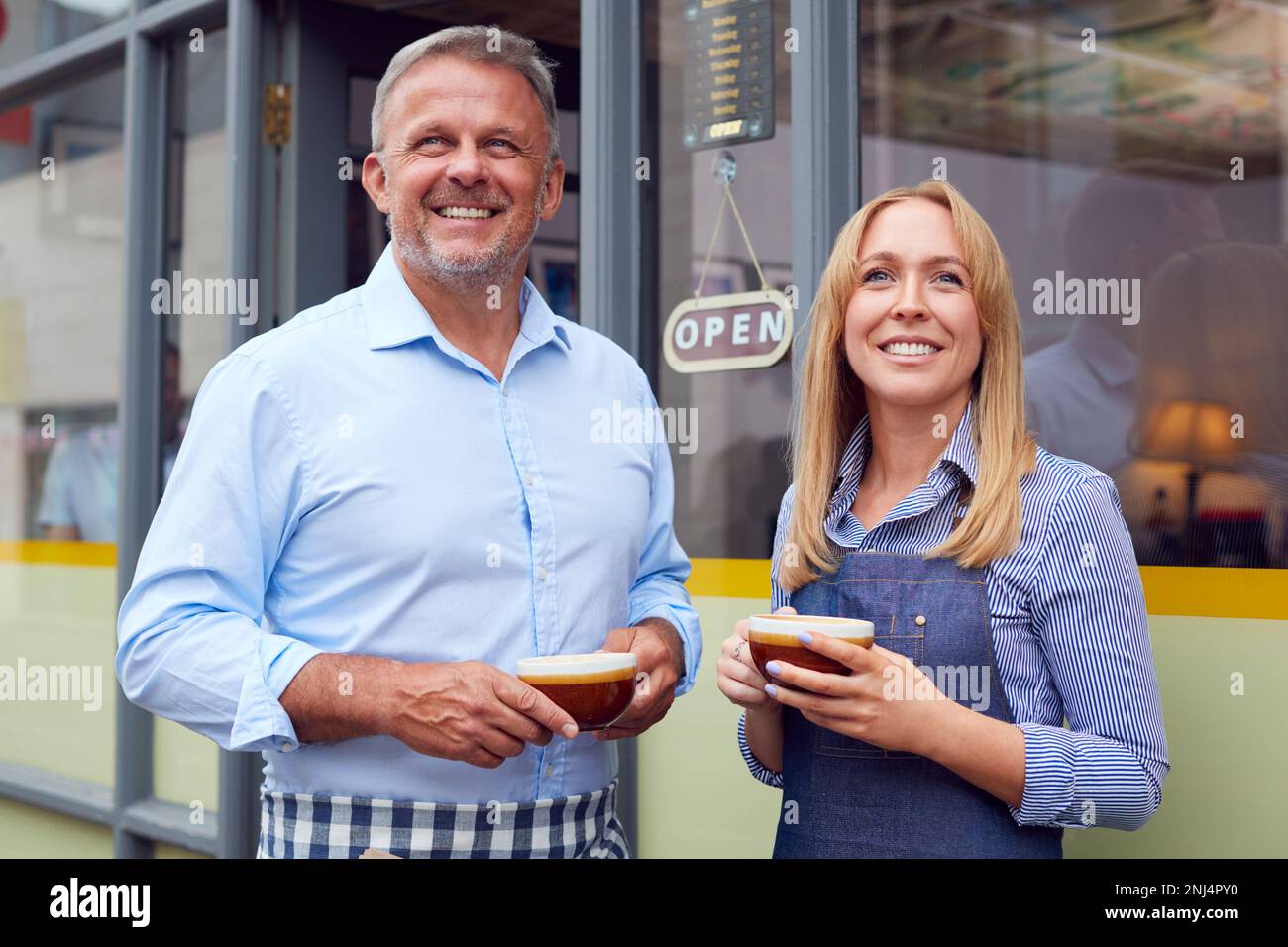 Male And Female Owners Or Staff Standing Outside Coffee Shop Holding ...