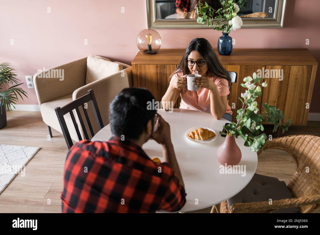Happy couple eating breakfast and talking at dining table in morning ...