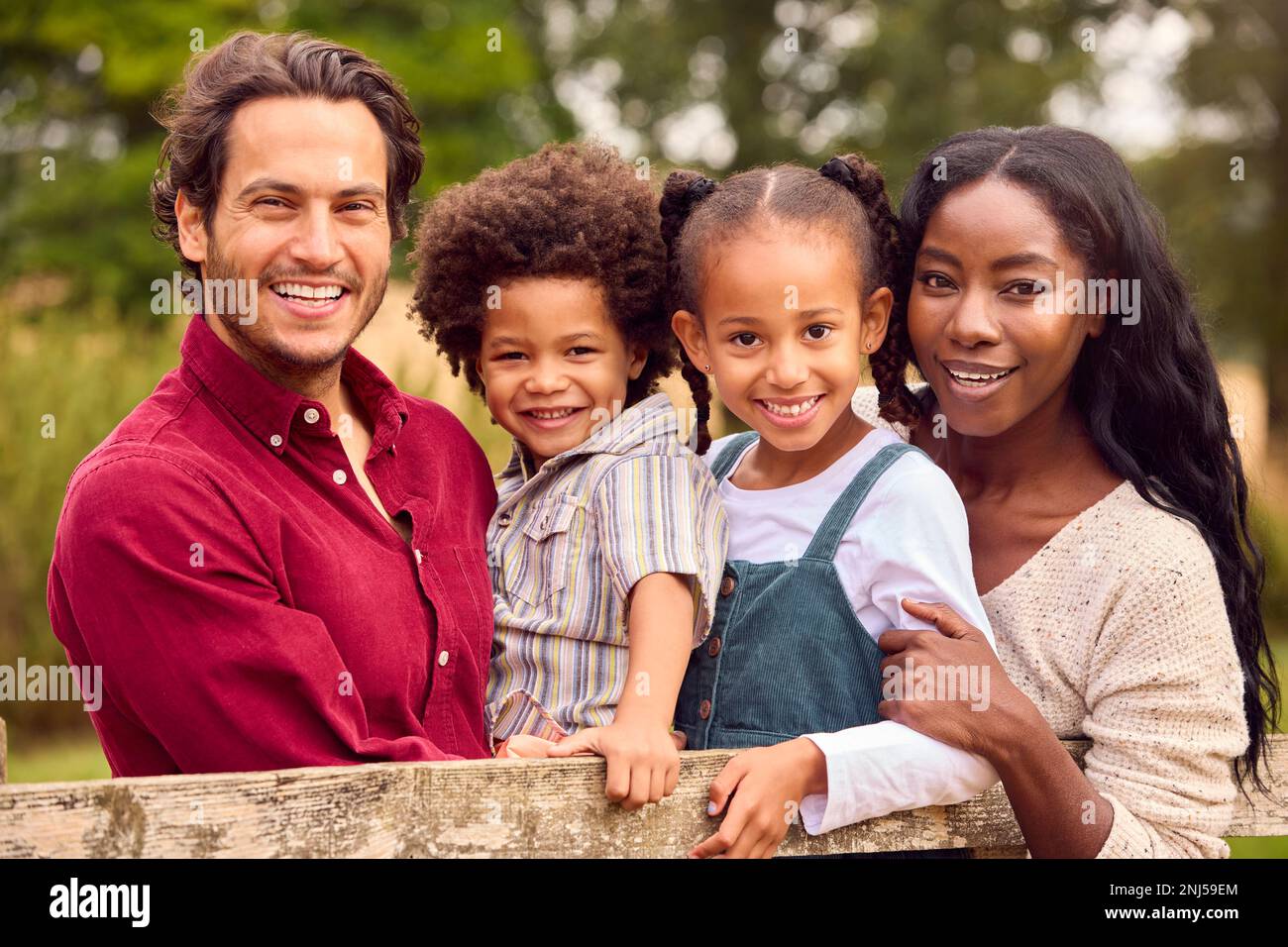 Portrait Of Loving Mixed Race Family Leaning On Fence On Walk In ...