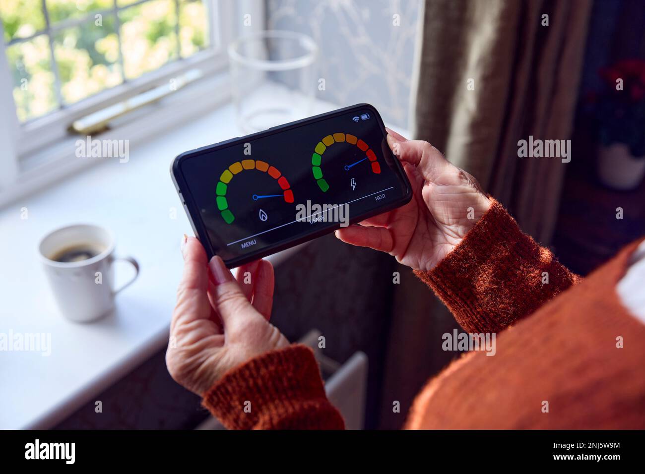 Senior Woman With Smart Meter Trying To Keep Warm By Radiator During ...