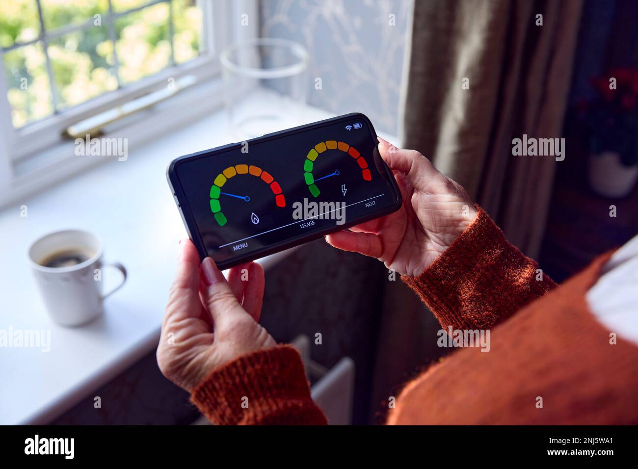 Senior Woman With Smart Meter Trying To Keep Warm By Radiator During ...