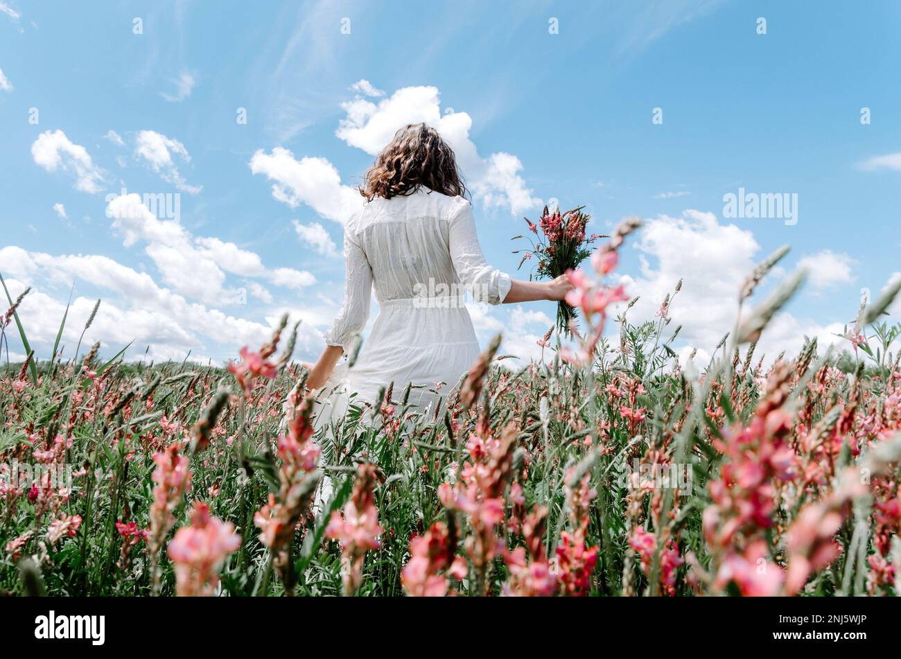 Back view of woman in long white dress with a wildflower bouquet in ...
