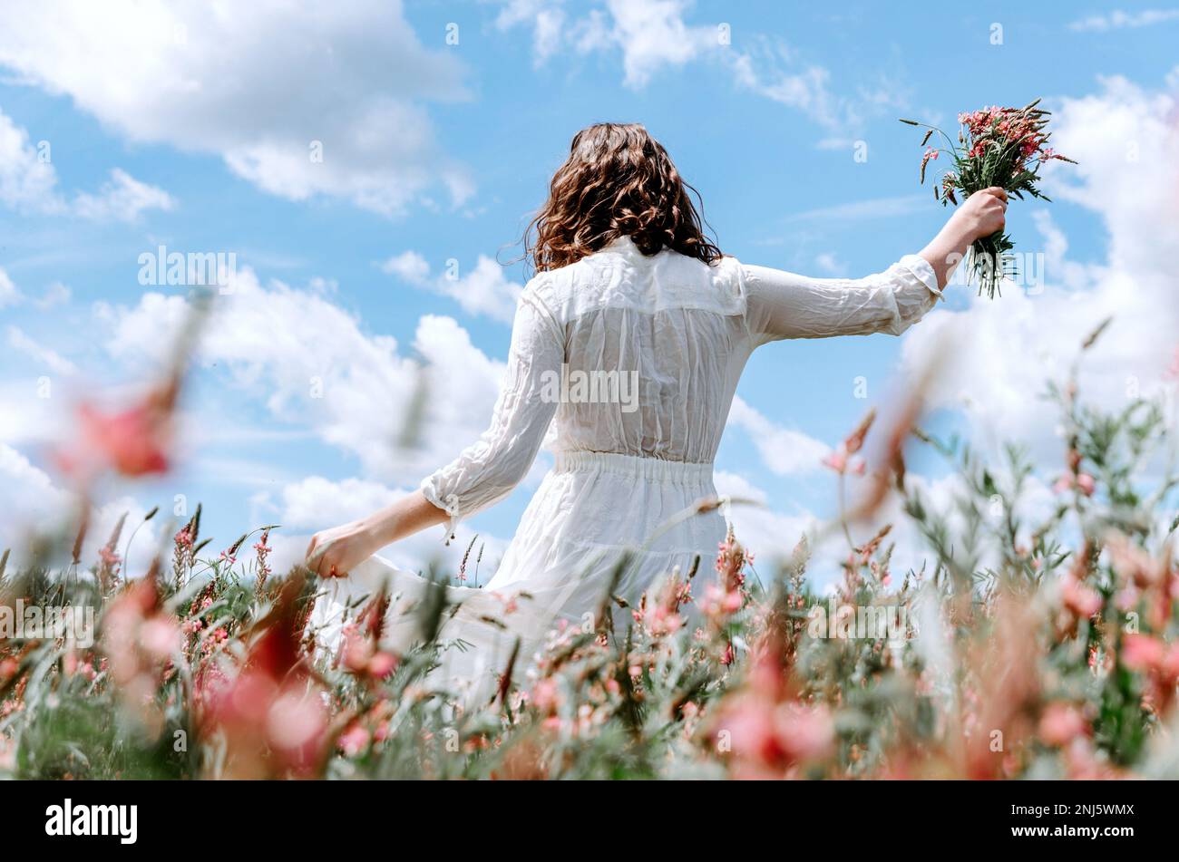 Back view of woman in long white dress with a wildflower bouquet in ...