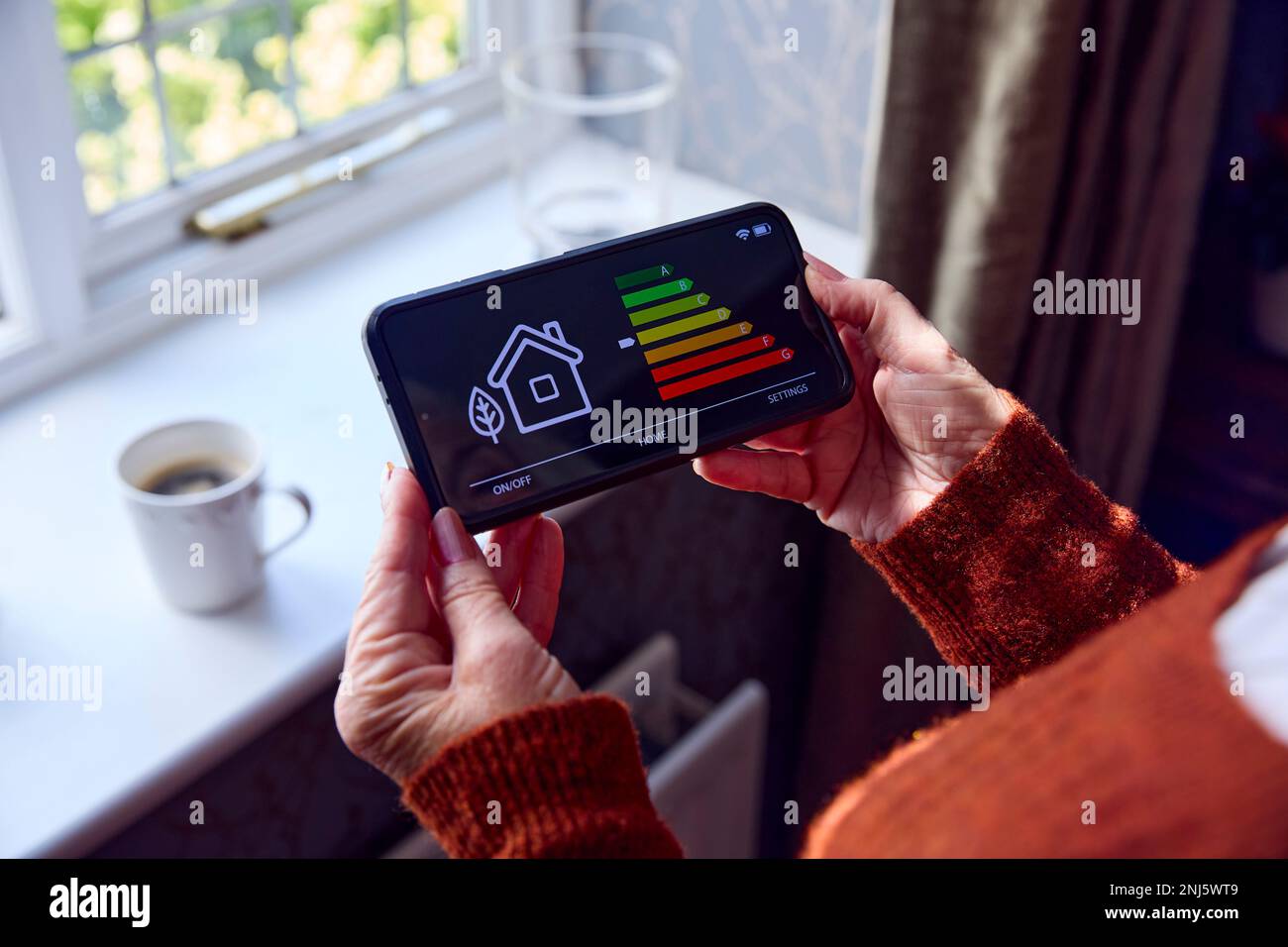 Senior Woman With Smart Meter Trying To Keep Warm By Radiator During ...