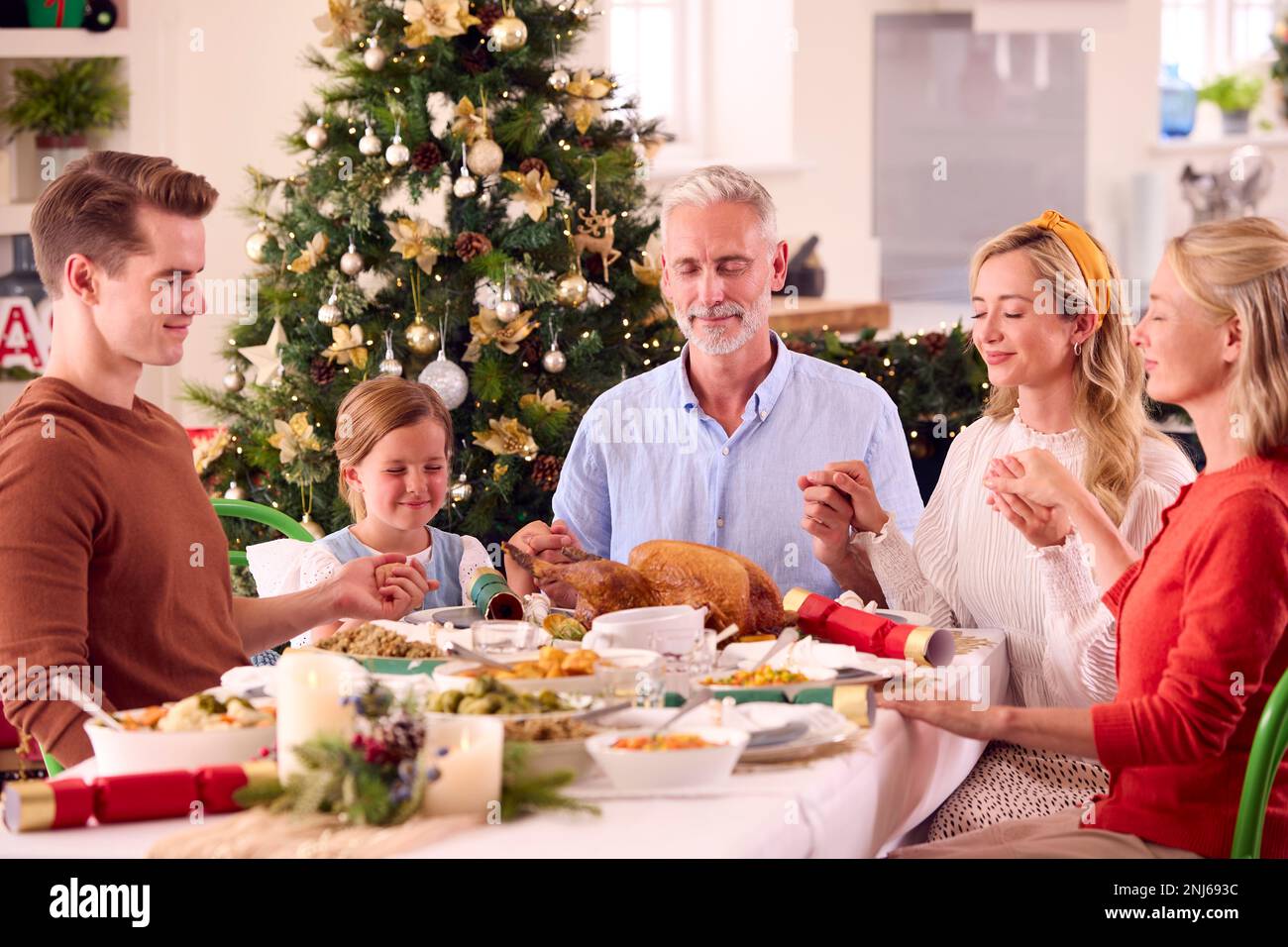 Multi-Generation Family Celebrating Christmas At Home Saying Prayer ...