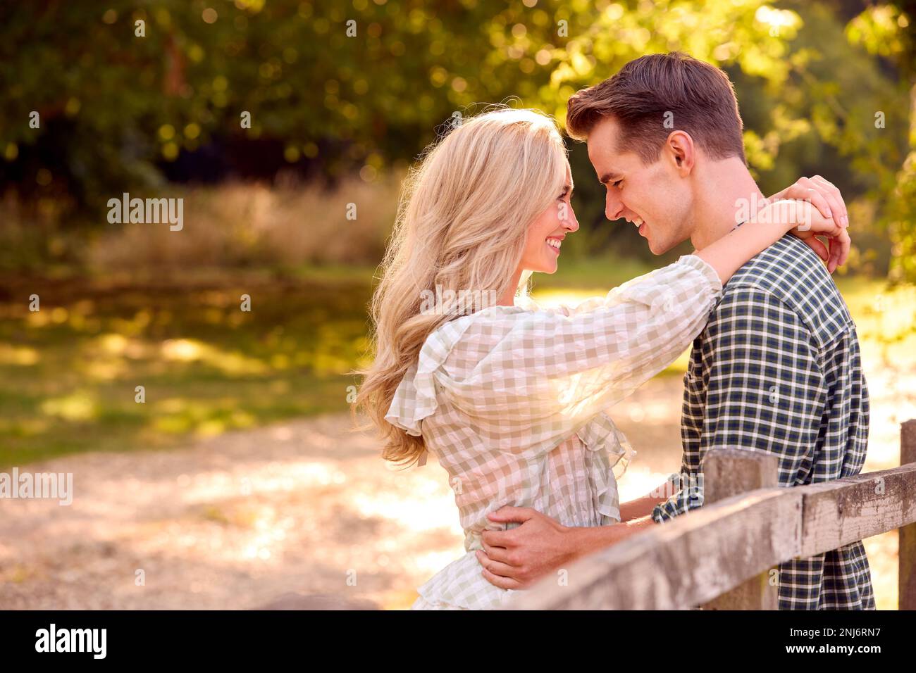 Loving Young Couple Leaning On Fence On Walk In Countryside Together ...