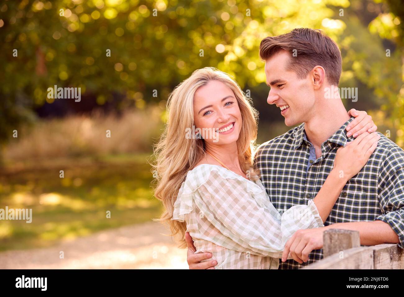 Portrait Of Loving Young Couple Leaning On Fence On Walk In Countryside ...