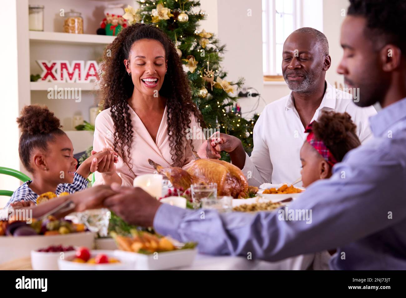 Multi-Generation Family Celebrating Christmas At Home Saying Prayer ...