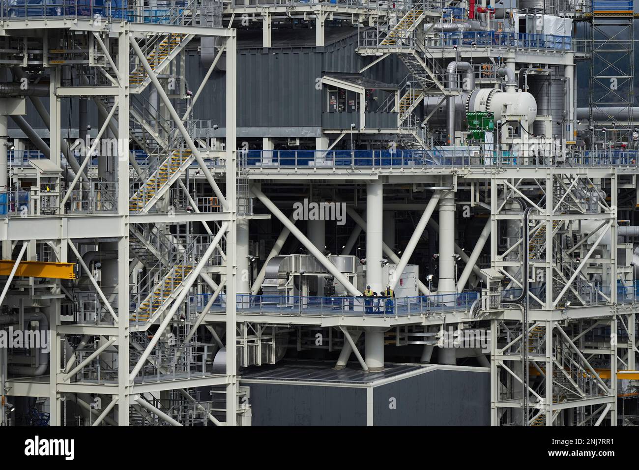 Workers stand on a platform on an LNG processing unit called a train ...