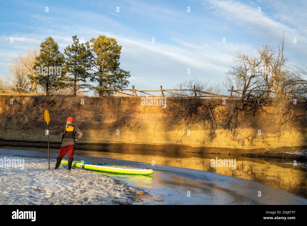 male paddler with inflatable stand up paddleboard on an icy shore of ...