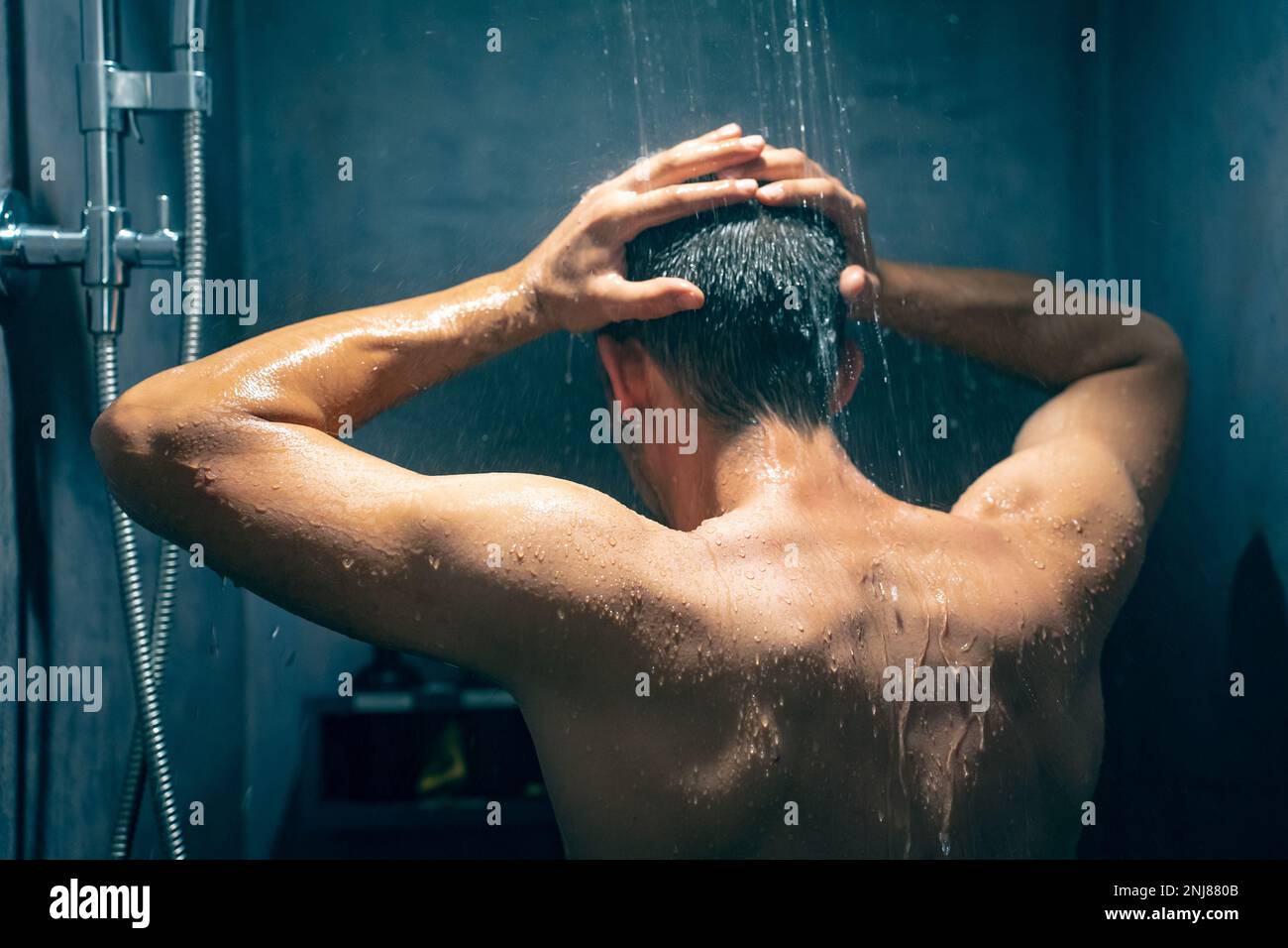 Man taking shower washing hair with shampoo product under water falling ...