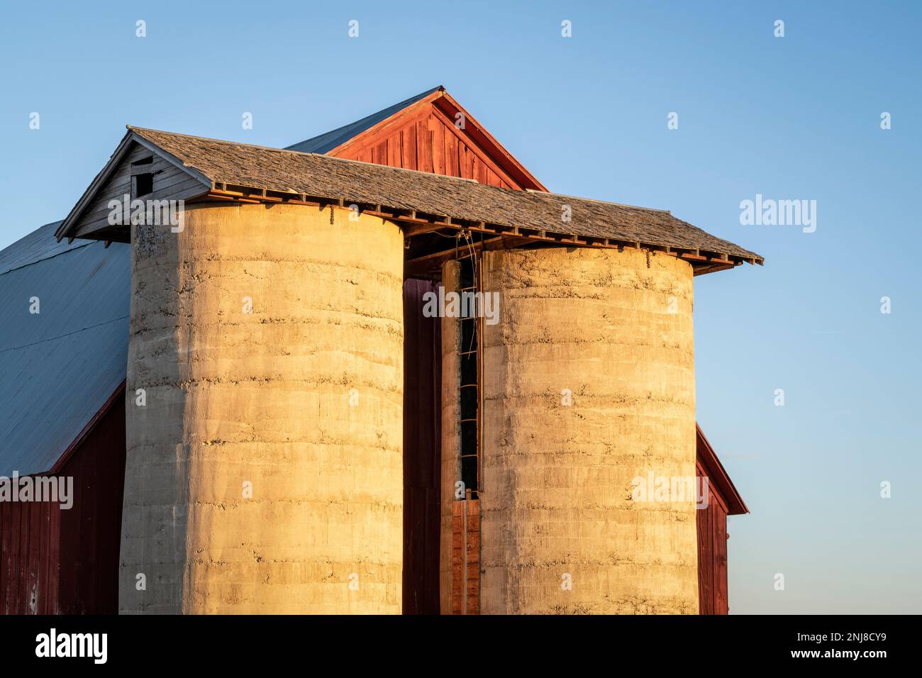 detail of old, weathered, red barn with twin silos in sunset light at ...
