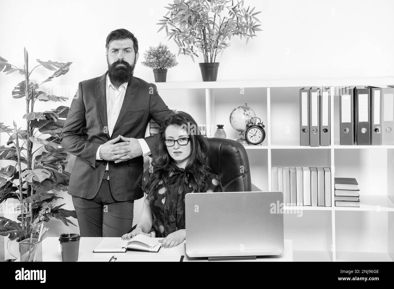 Serious man in suit standing over career woman working at office desk ...