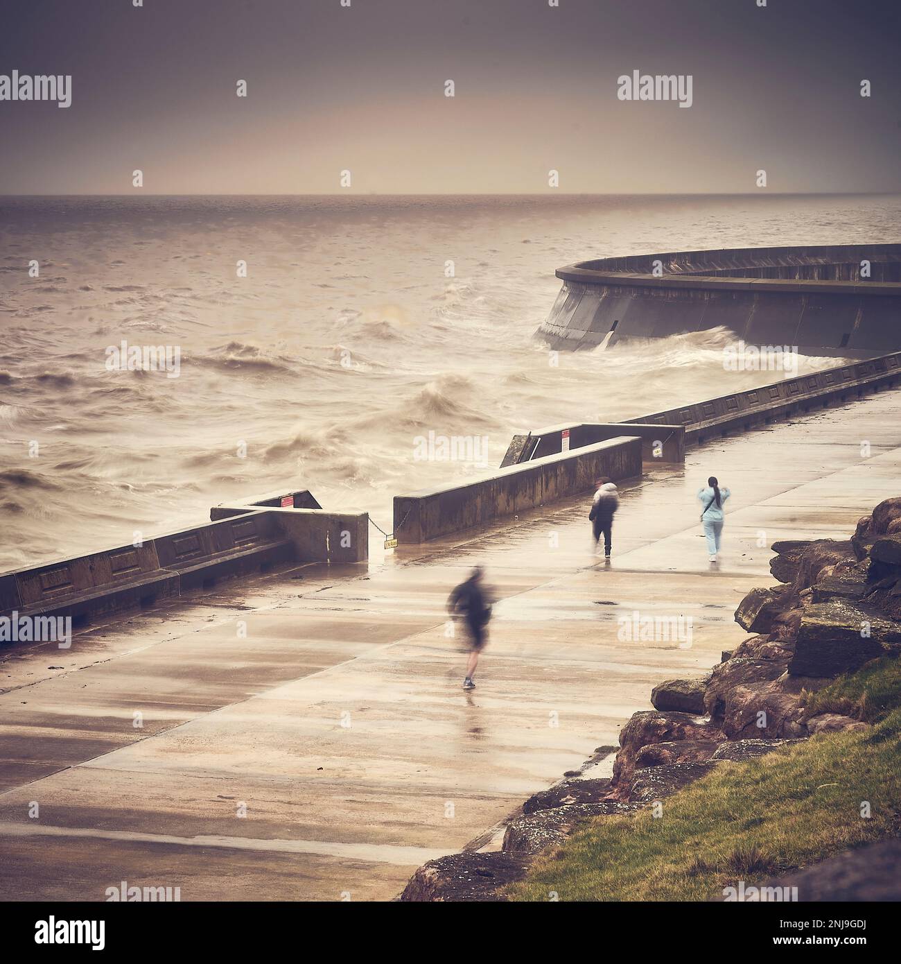 Walkers and runner on Blackpool lower promenade at high tide during ...