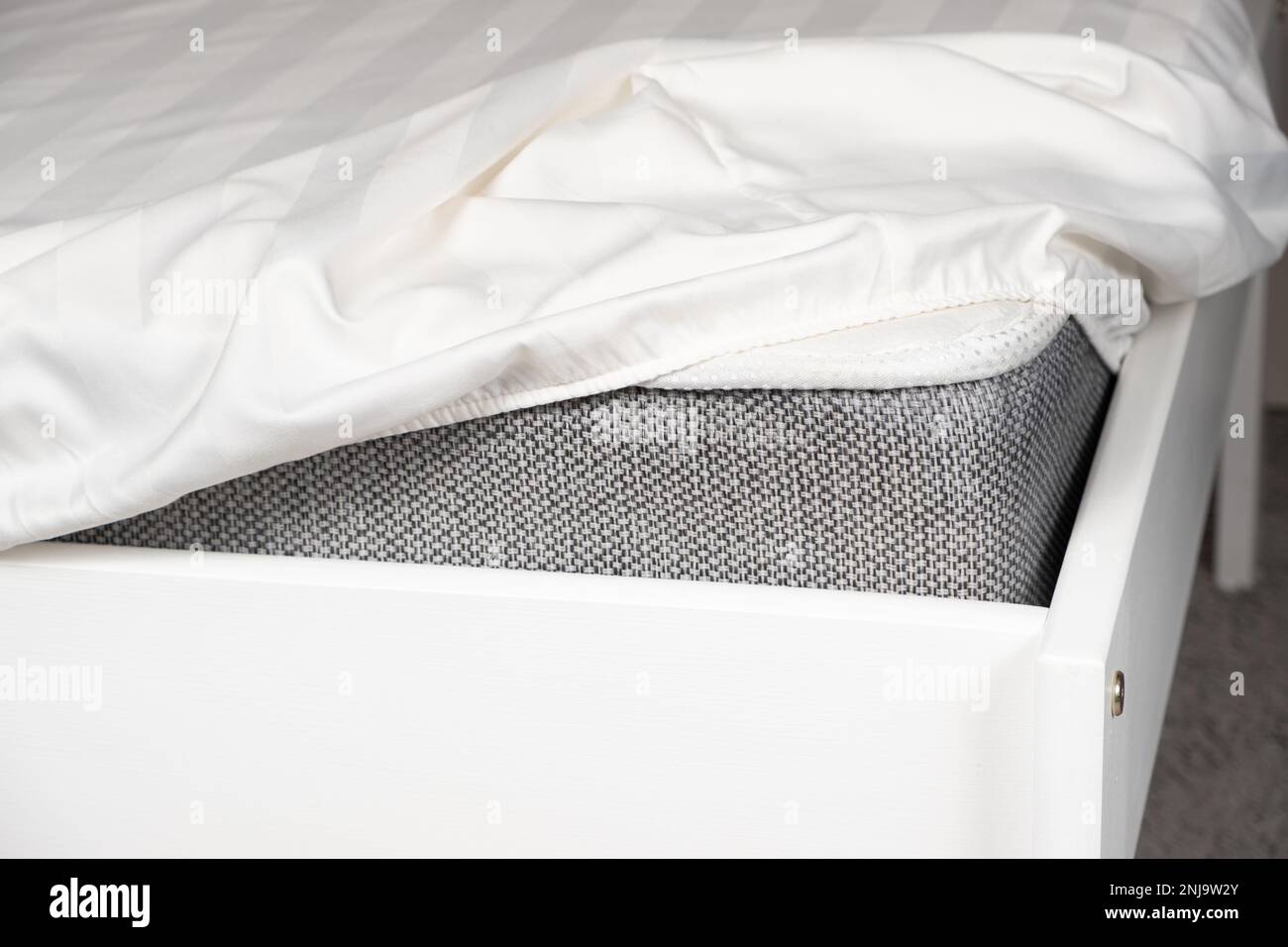 White satin sheet on an elastic band on the mattress. Bed linen on the ...