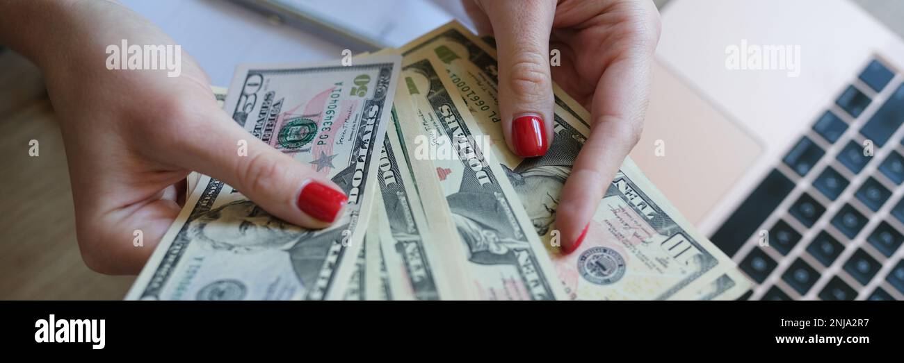 Woman hands holding dollar bills earned by working from laptop at home ...