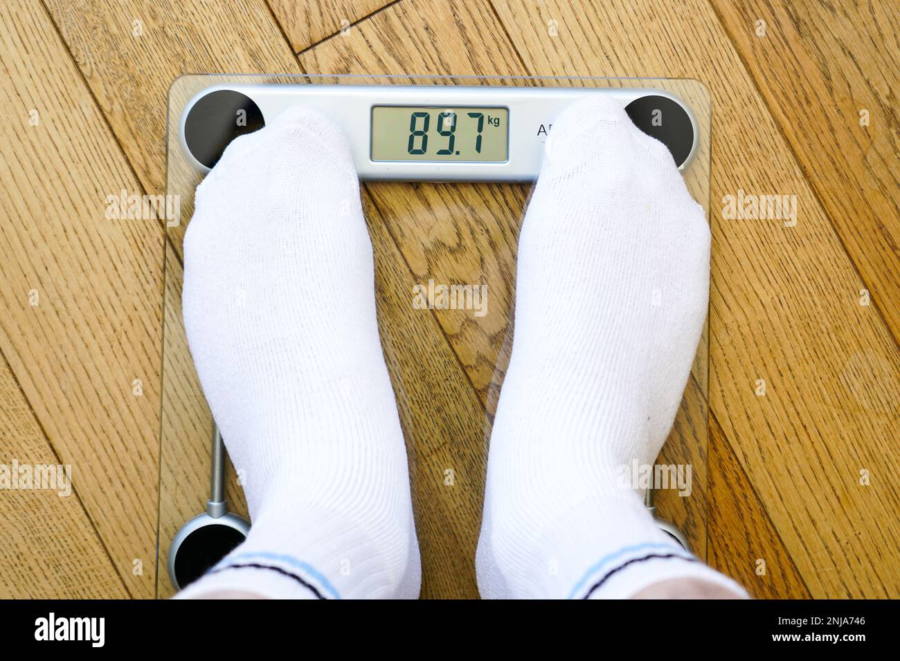 A man in white socks weighing himself on a transparent electronic floor scale, the weight ...