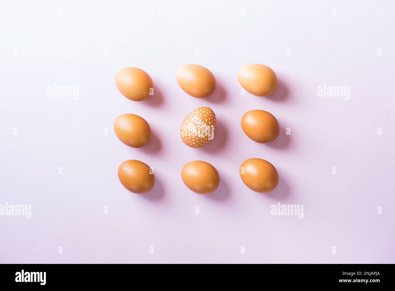 Nine brown eggs flat lay on purple background with one Happy Easter ...