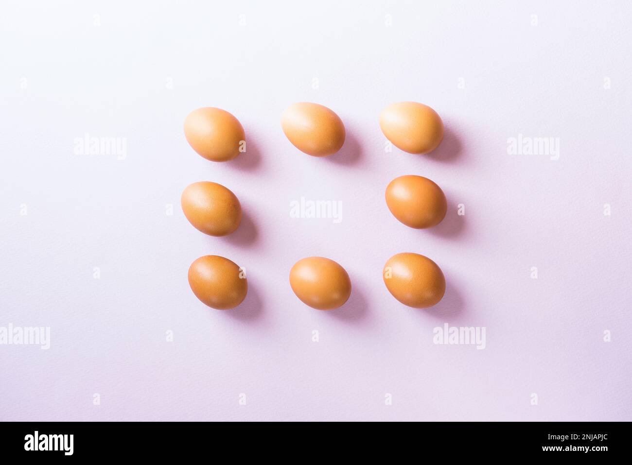 Nine brown eggs flat lay on purple background with copy space on center ...