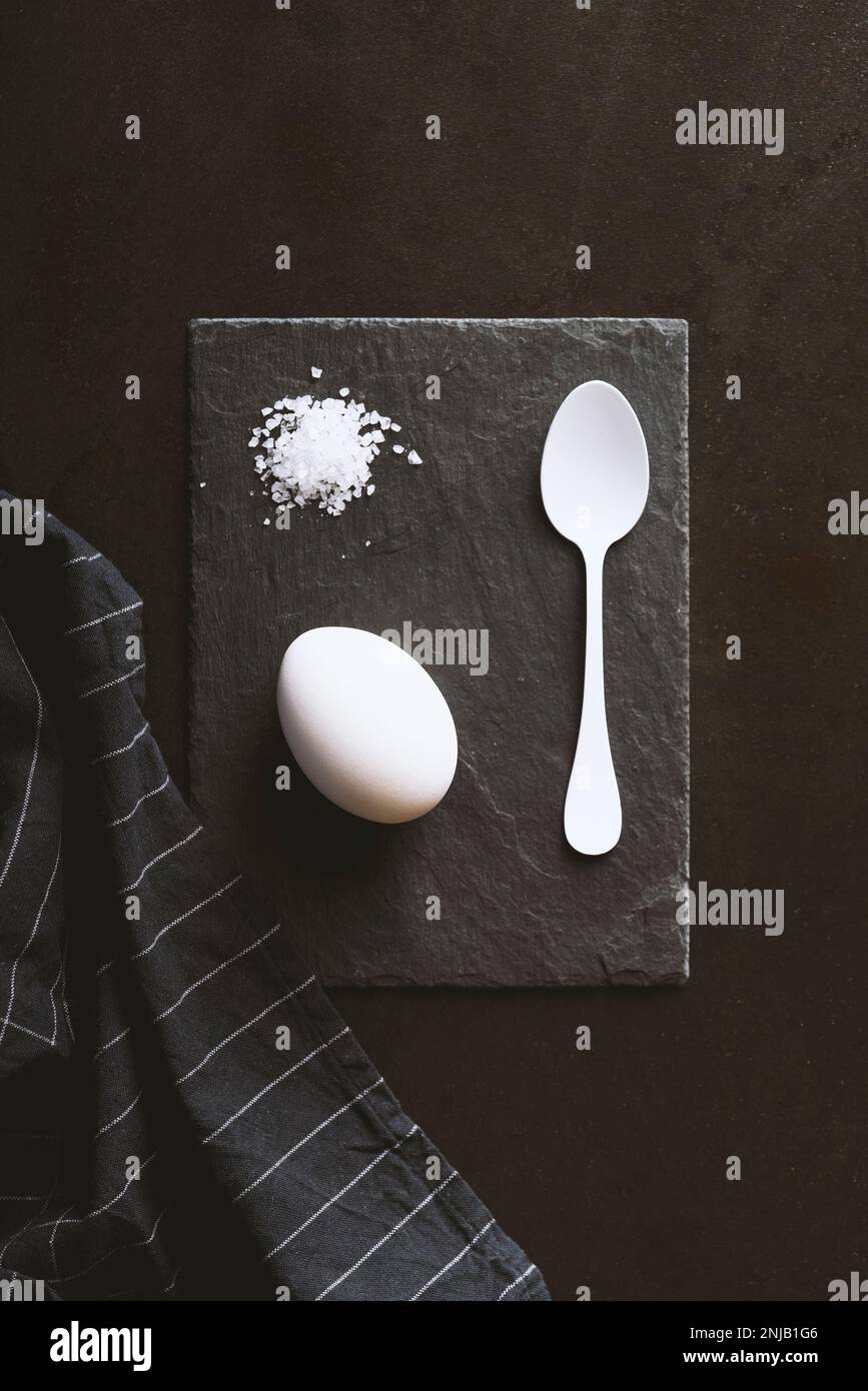 Egg and a pinch of salt with a spoon on plate. White objects flat lay ...