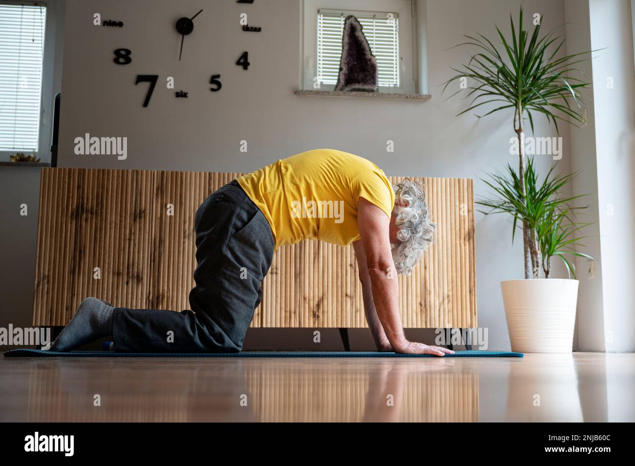 Male pensioner in yellow shirt making a pilates cat pose while working ...