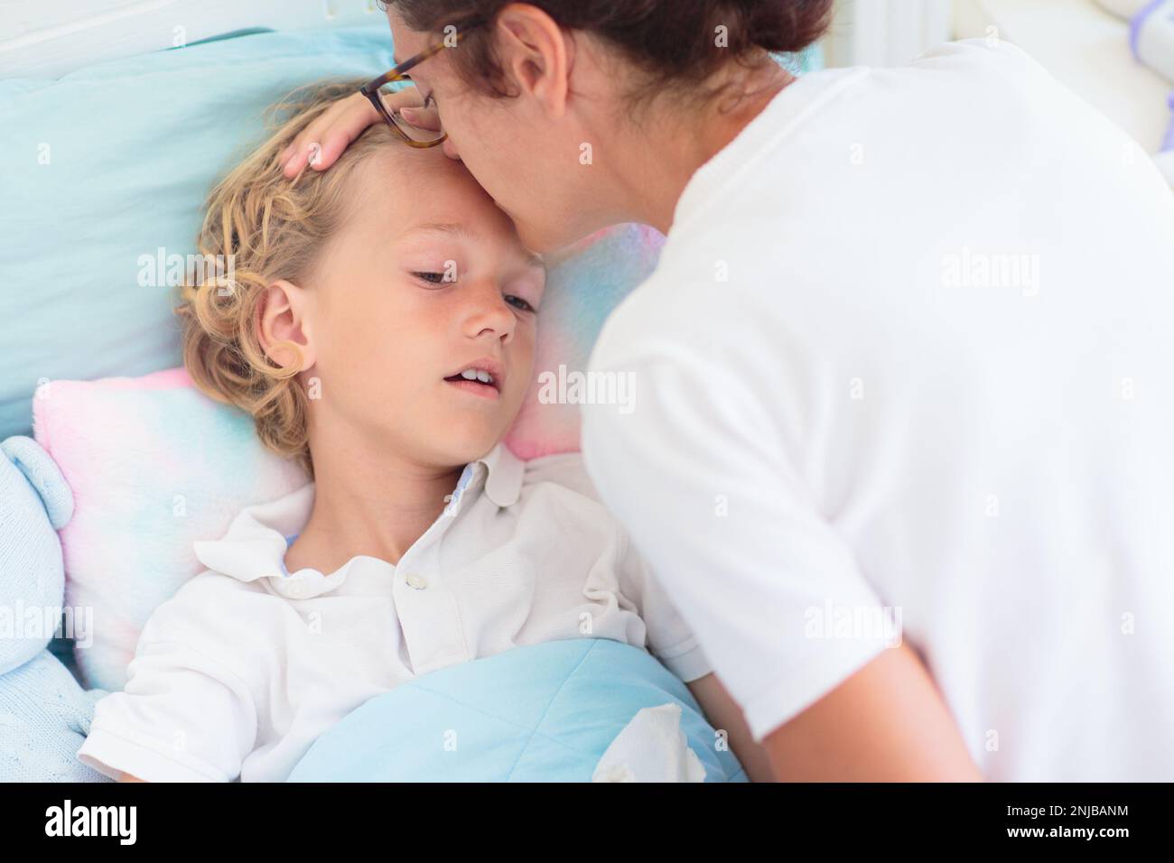 Sick child in bed. Mother checking on unwell kid. Little boy having fever feeling ill. Mom with ...