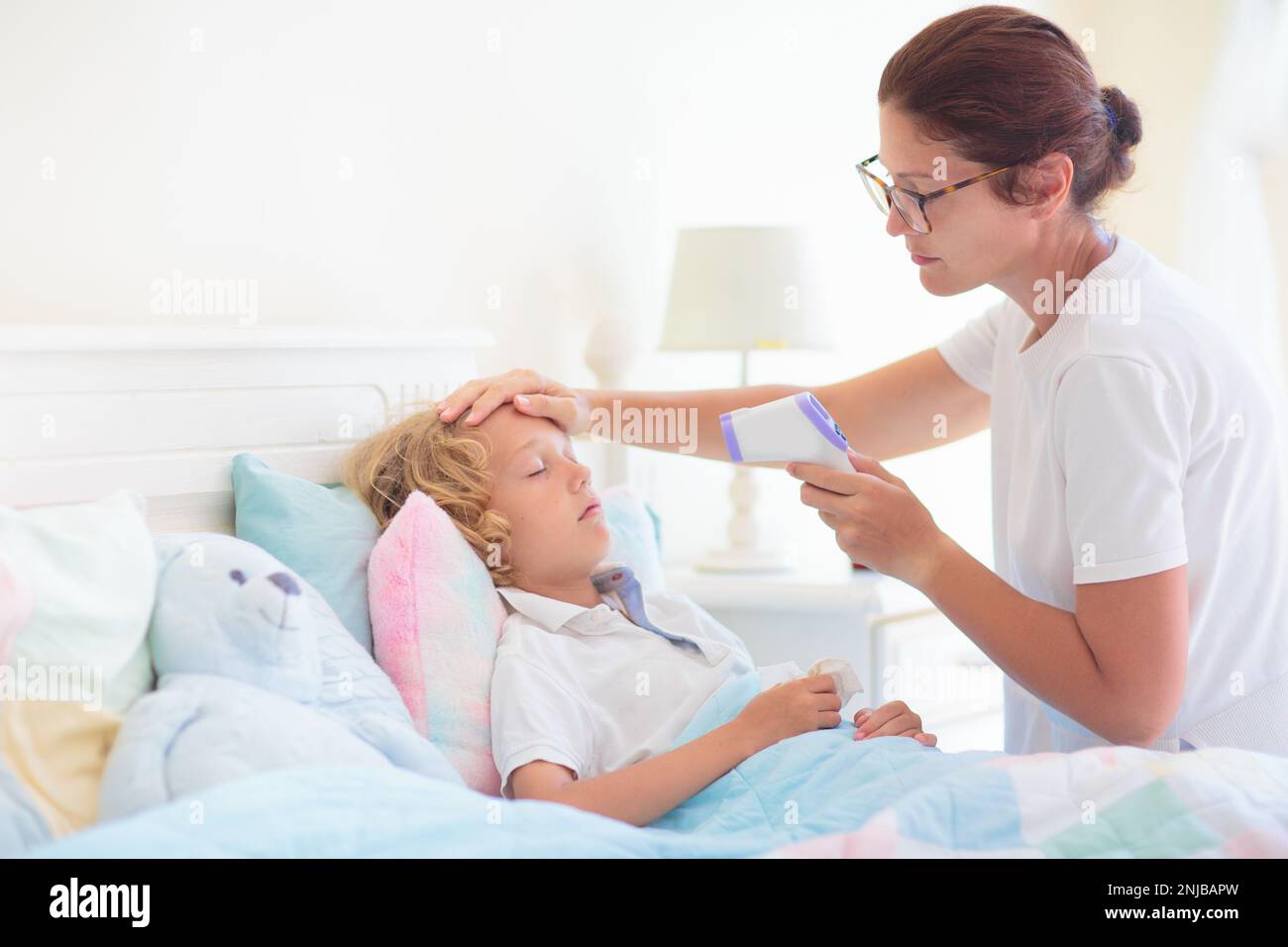 Sick child in bed. Mother checking on unwell kid. Little boy having fever feeling ill. Mom with ...