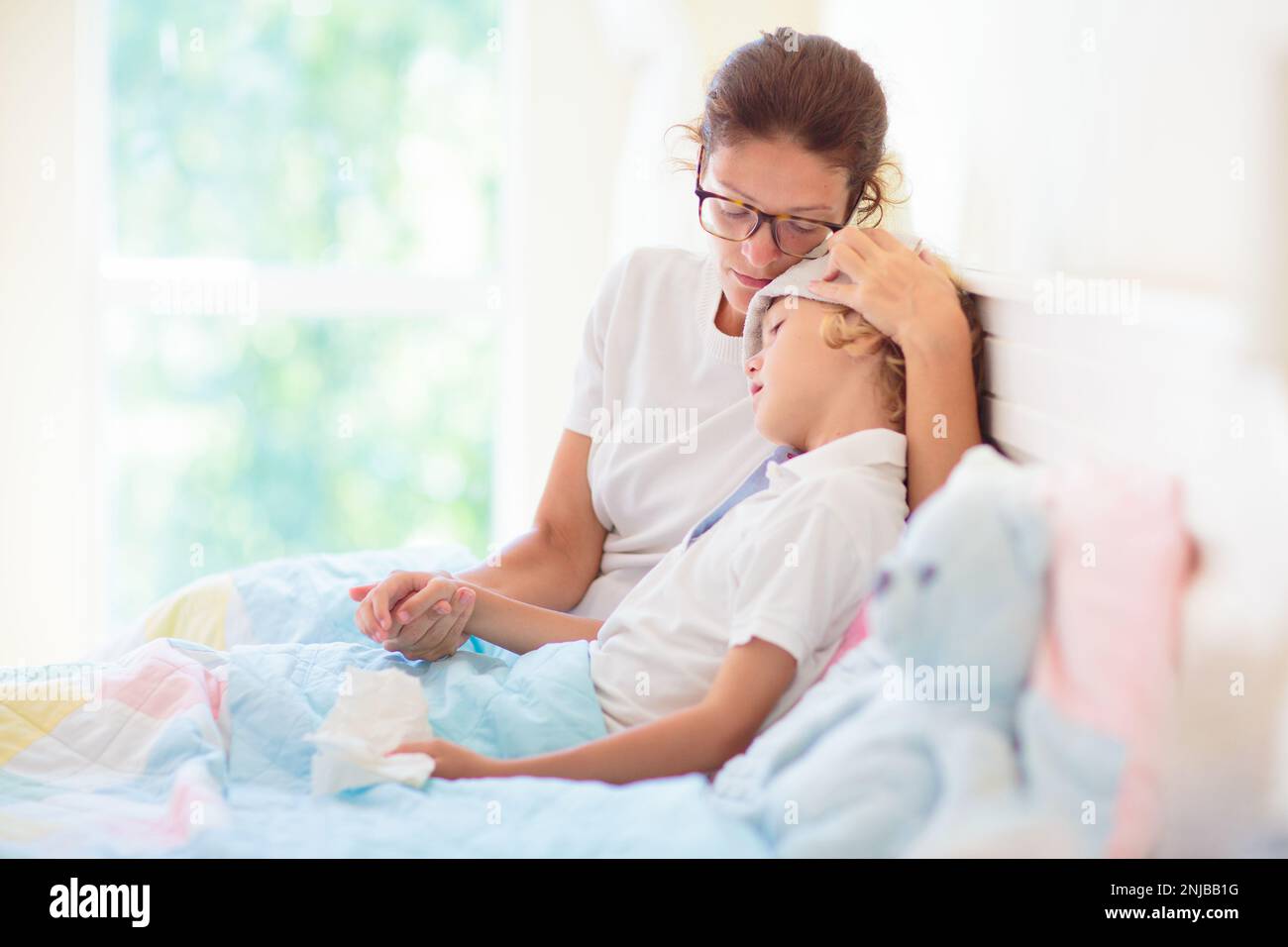 Sick child in bed. Mother checking on unwell kid. Little boy having fever feeling ill. Mom with ...