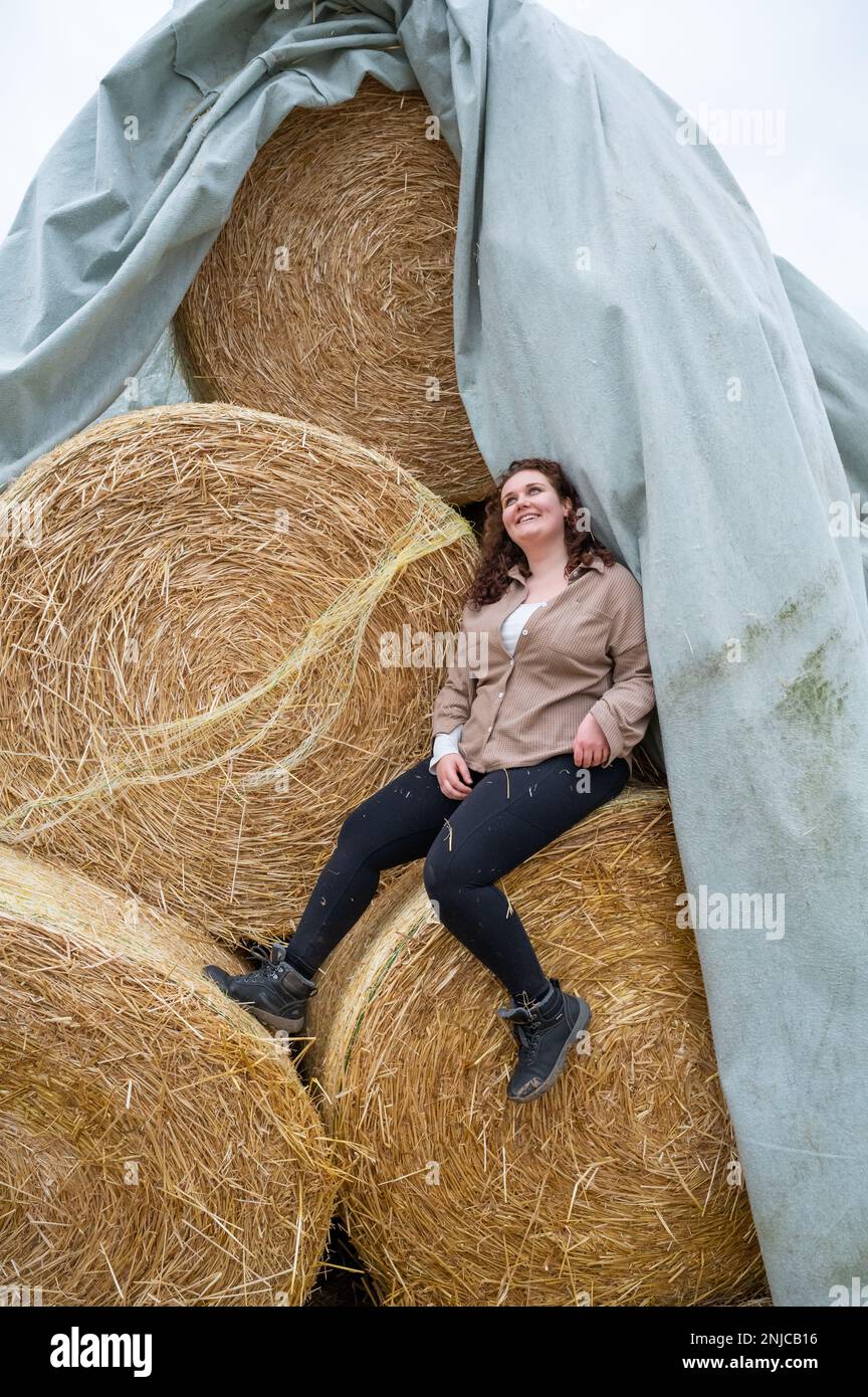 Women with brown curly hair sitting on stacked hay balls, smiling and ...