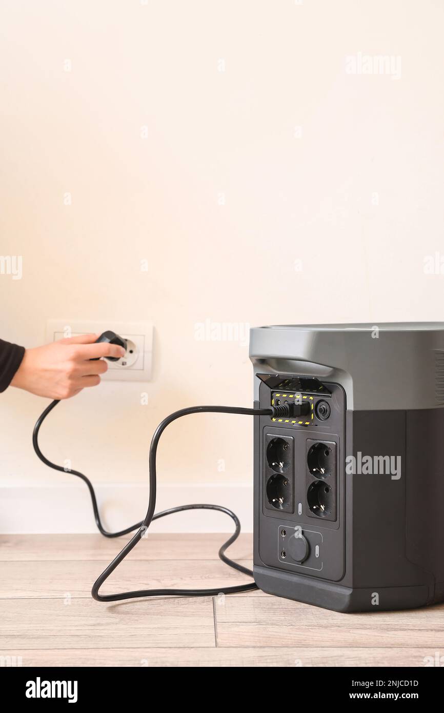 Woman inserting plug of portable solar station into socket at home ...