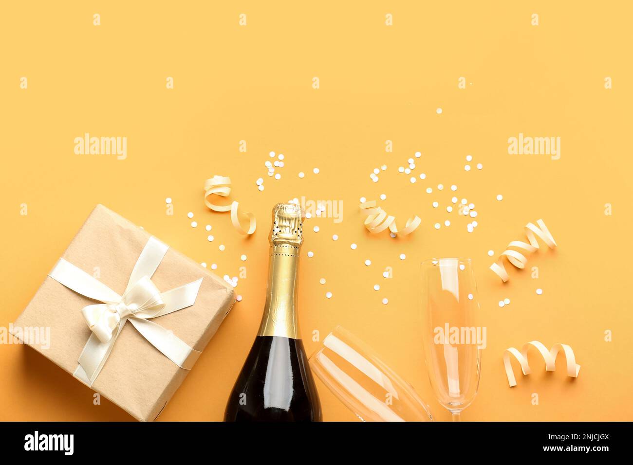 Bottle of champagne, gift box, glasses and serpentine on orange ...