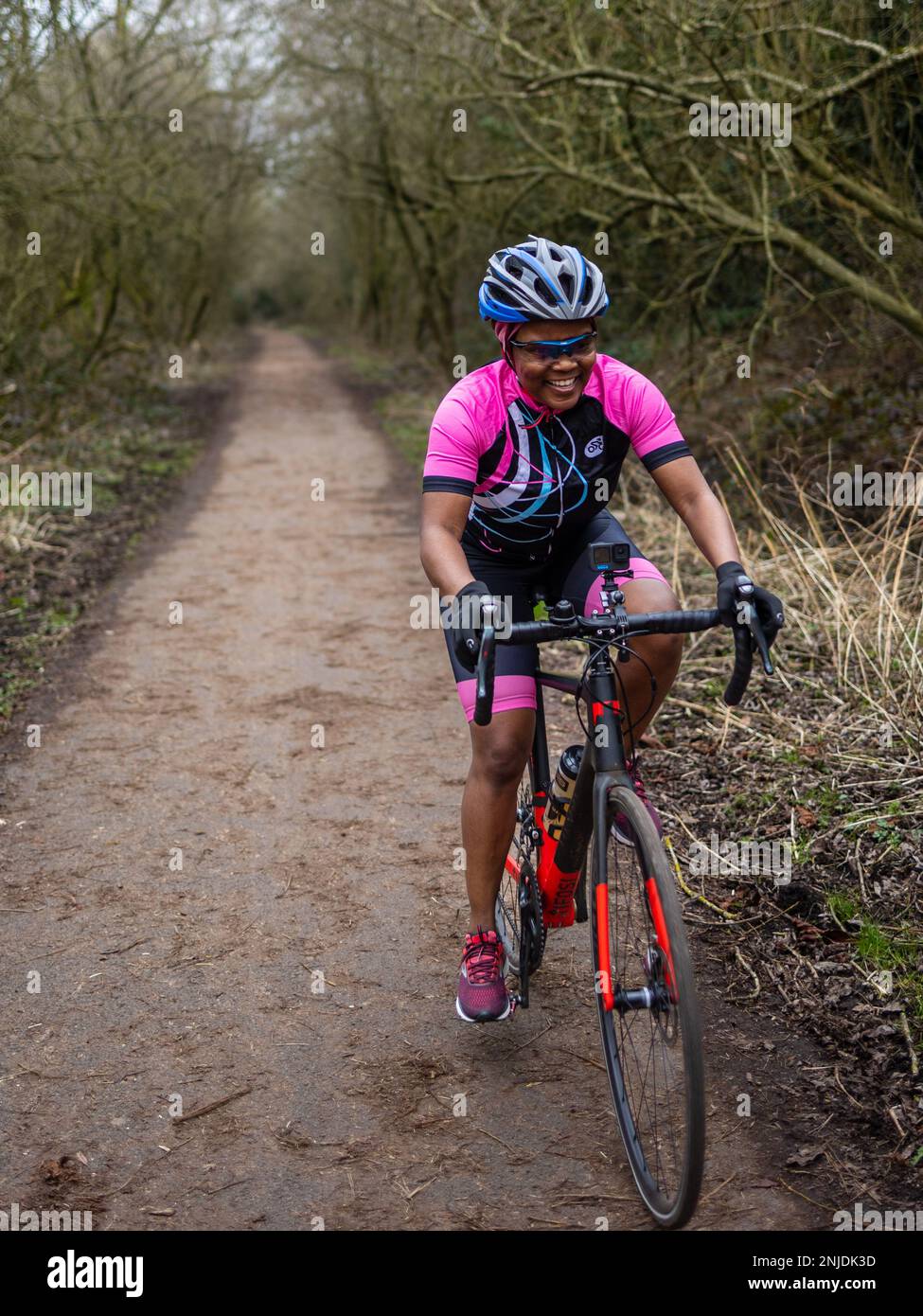 A smiling female cyclist walks her bike along a forest trail, embracing ...
