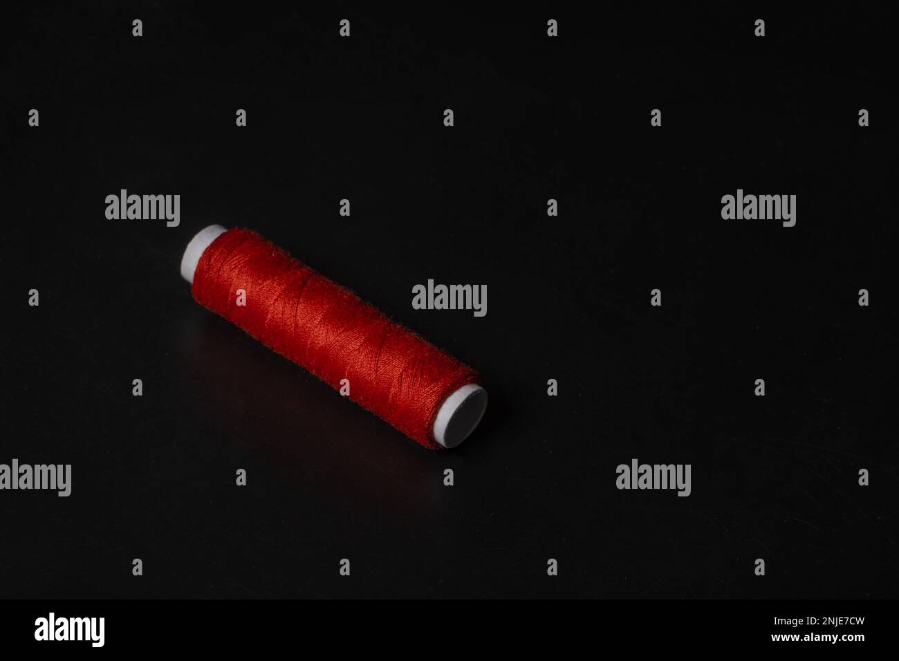 A lonely spool of red thread on a black surface Stock Photo - Alamy