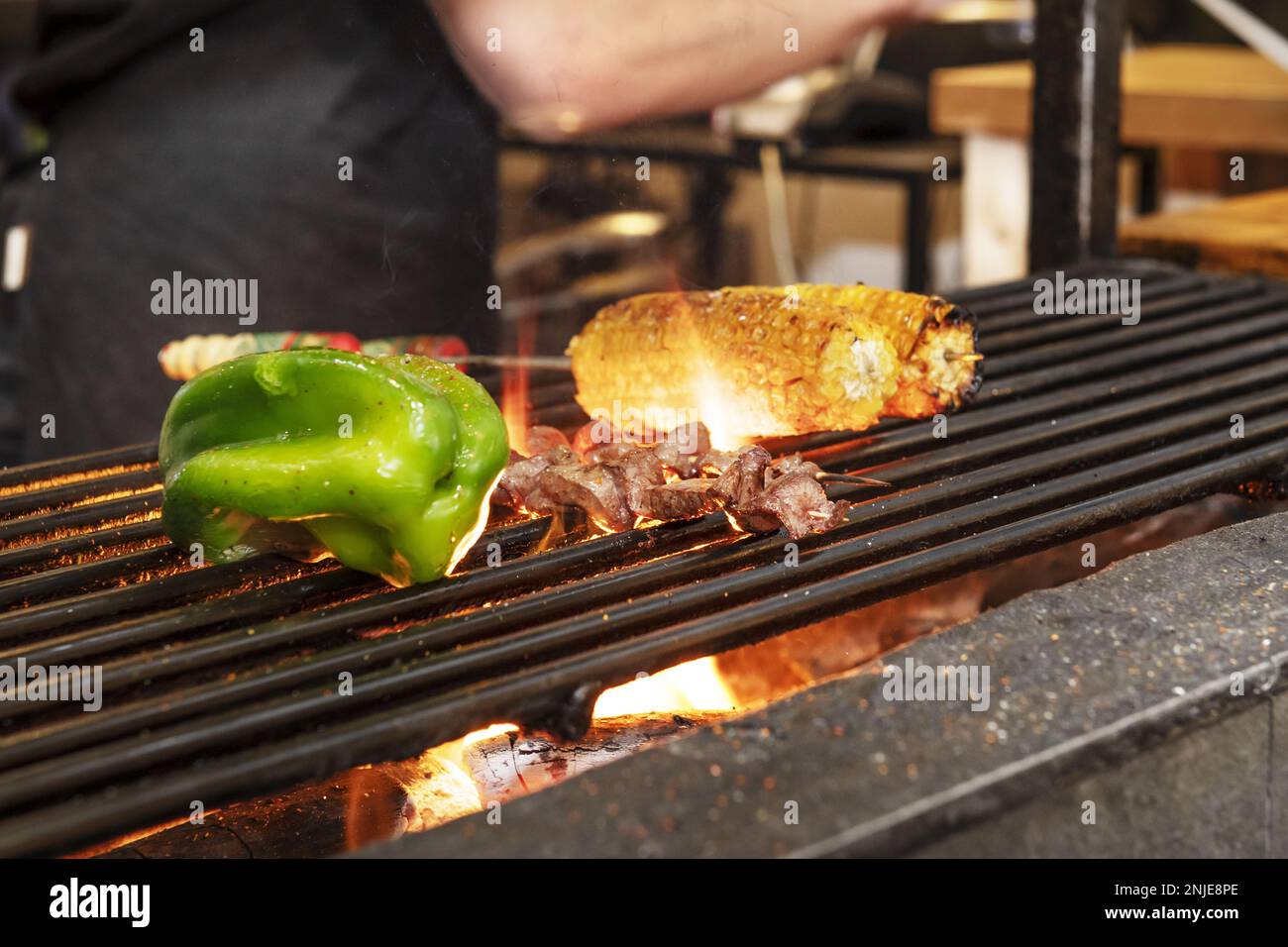 A chef spinning meat skewers as they cook over wooden coals alongside ...