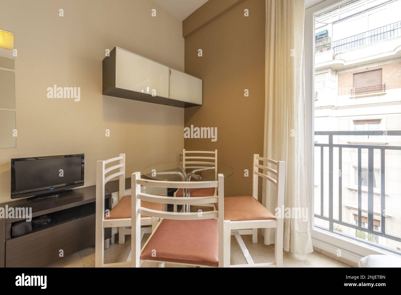 Round glass dining table with white wooden chairs next to a balcony ...