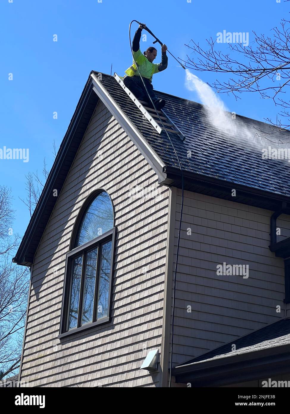 Latino workman powerwashing the roof of a residential home to remove ...