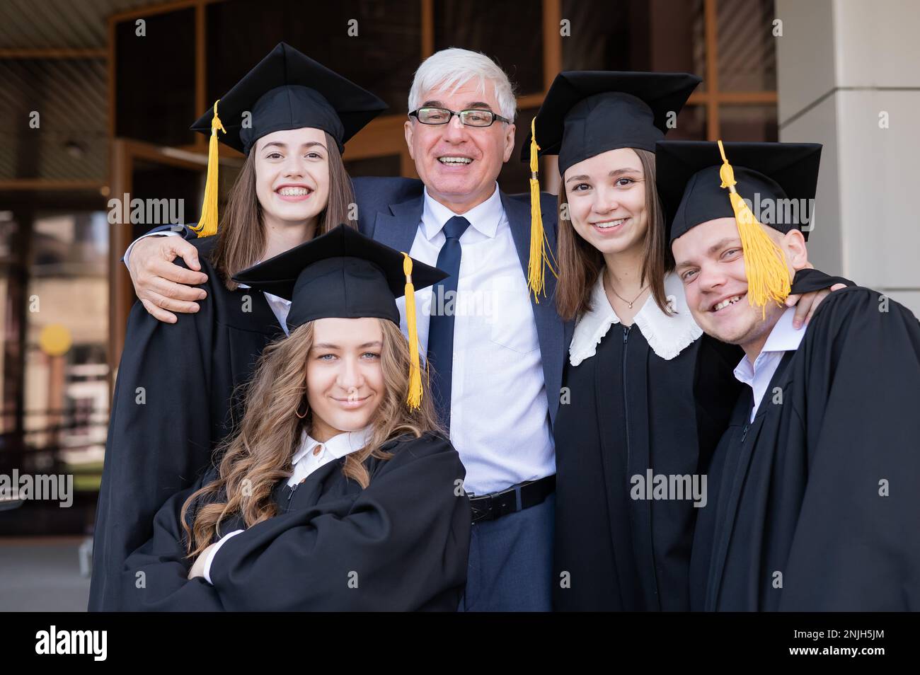 A gray-haired male teacher congratulates students on their graduation ...