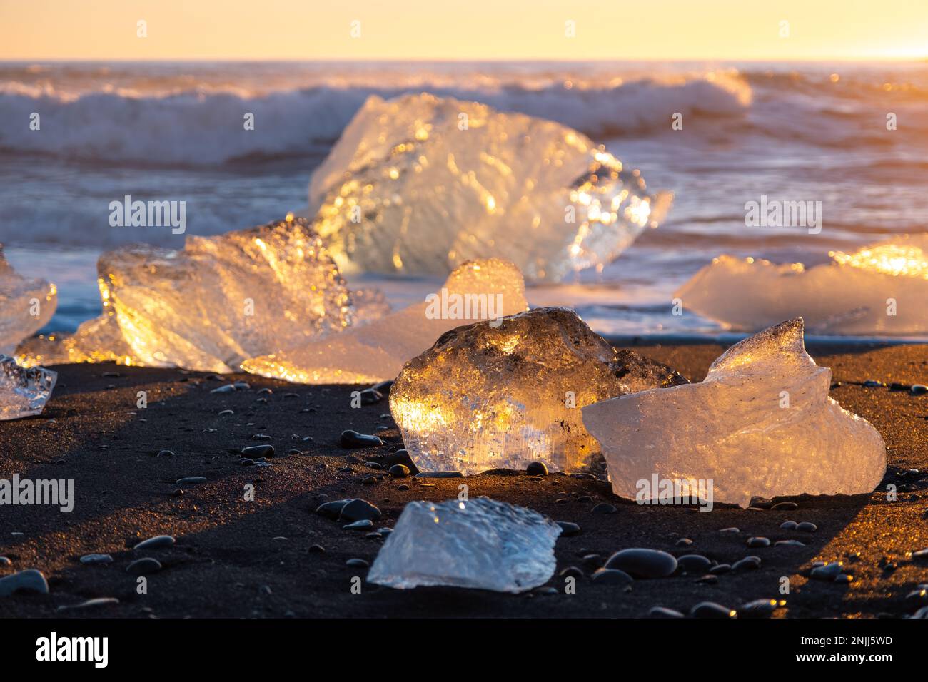 Pure glacier ice shining at sunset. Black volcanic sand at ocean coast ...